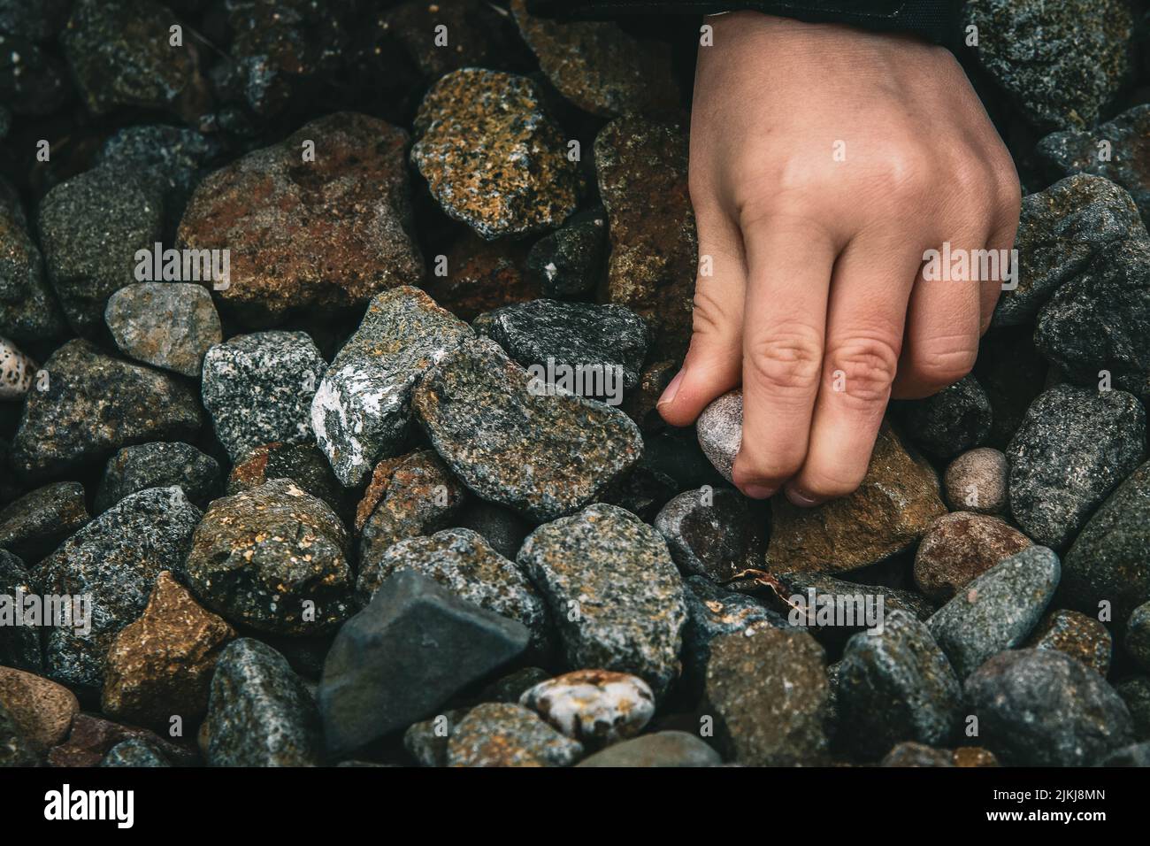 A closeup shot of an adult hand picking up a small gravel off the ...