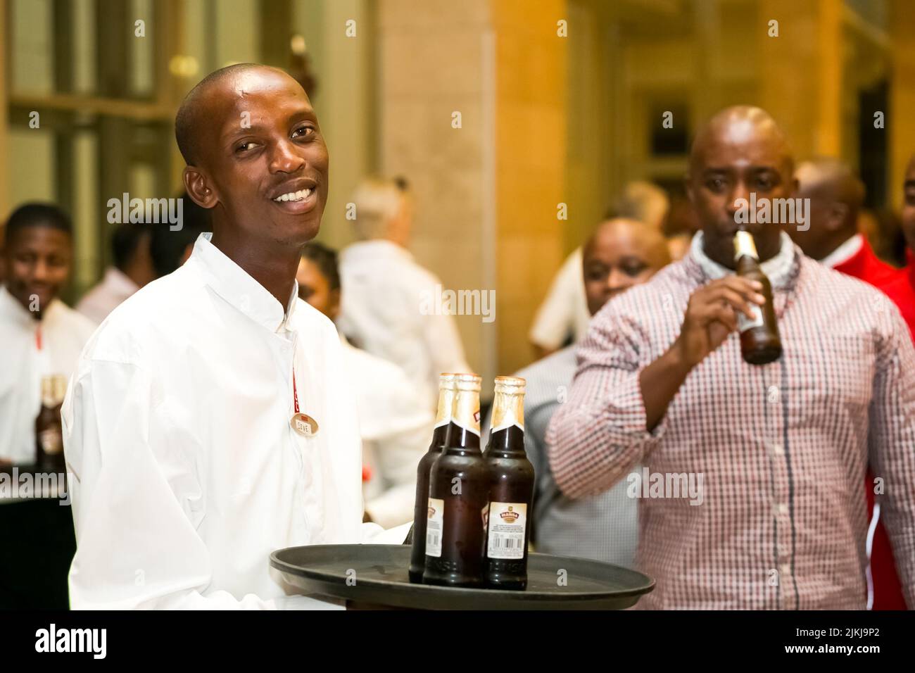 An African waiter holding drinks tray for guests at an indoor party ...