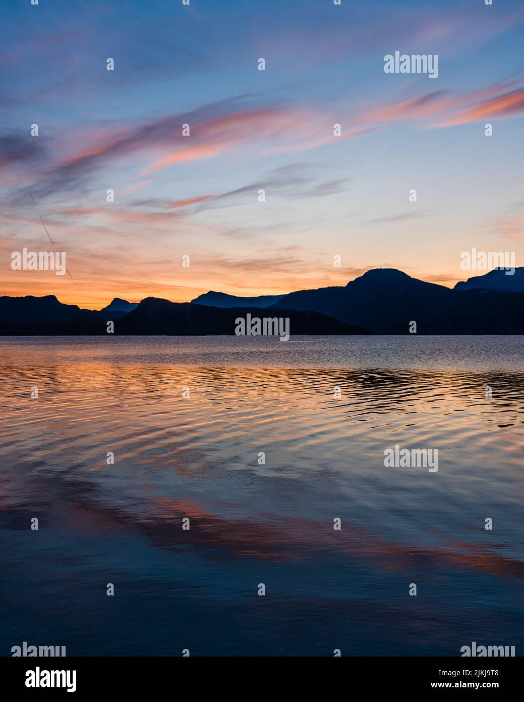 A vertical breathtaking view of lakeside mountains on the sunset sky ...