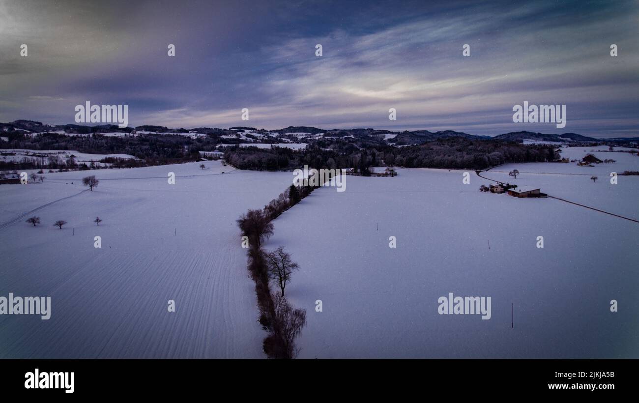An aerial view of a snowy landscape with a road and houses on a gloomy ...