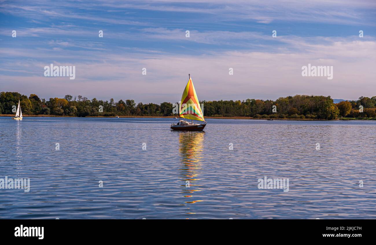 A small boat sailing in a body of water with trees and a light cloudy ...