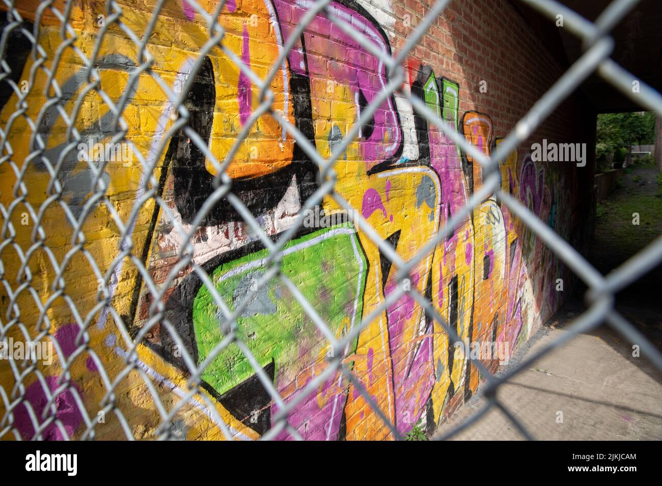 A wall of colorful graffiti seen behind a metallic chained fence Stock ...