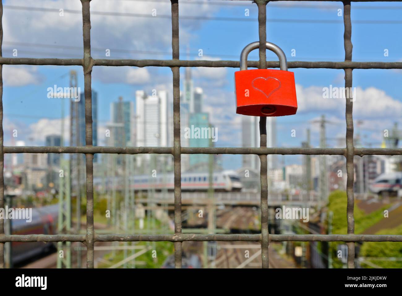 A red lock with a heart fixed on a fence with the blurry skyline of ...