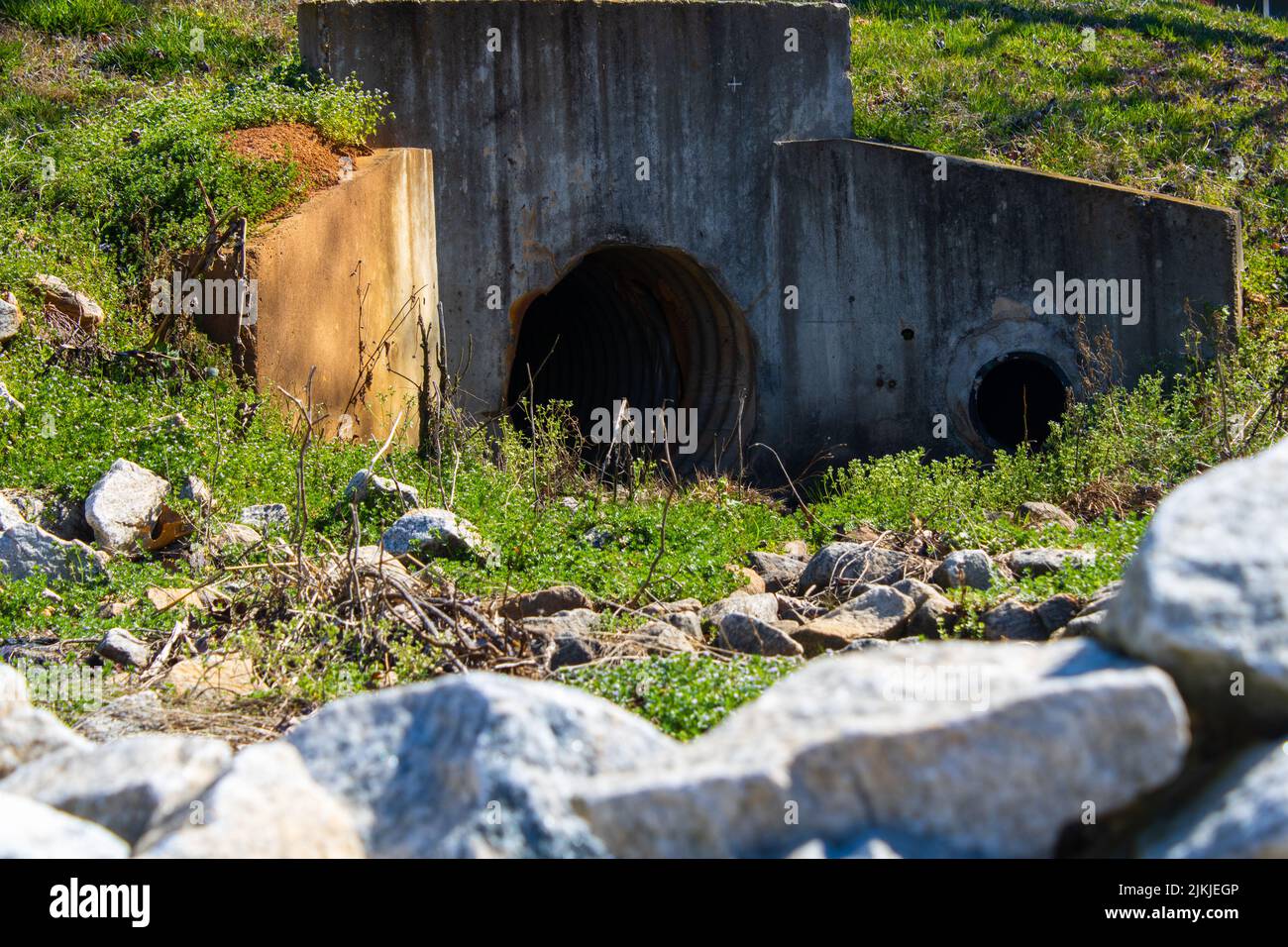 An opening of a sewer tunnel surrounded by rocks and green plants Stock ...