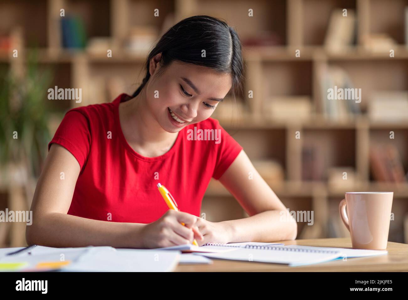 Cheerful pretty teenage japanese female doing homework alone, enjoy ...