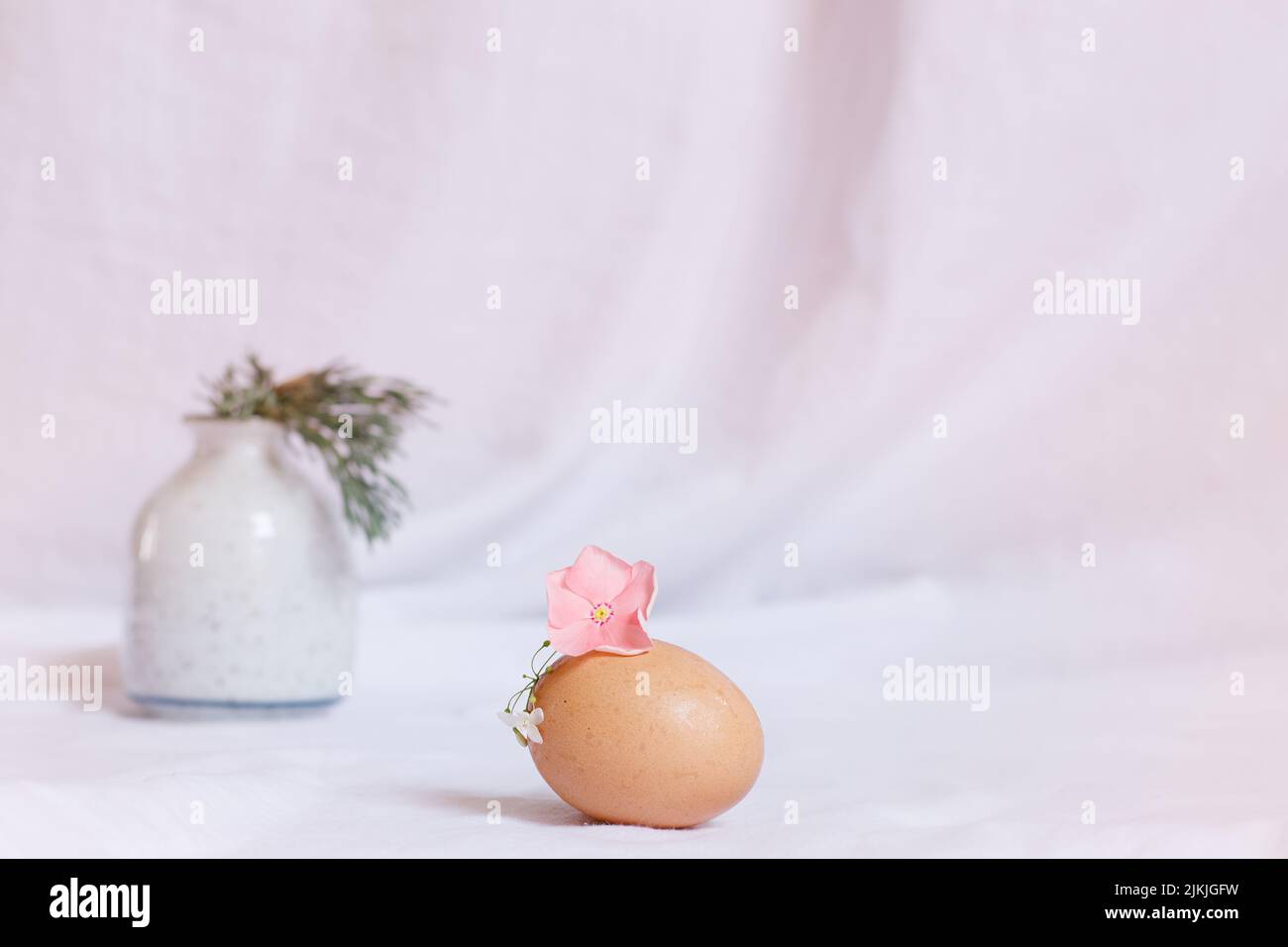 An Easter wet egg with spring flower on it next to a vase on a white ...