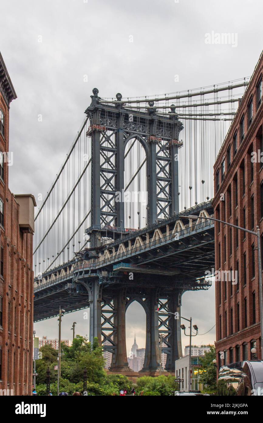 The Manhattan Bridge between two red brick buildings on a cloudy day in ...