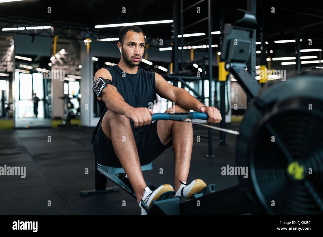 Sporty Young Black Man Exercising With Rowing Machine At Modern Gym ...