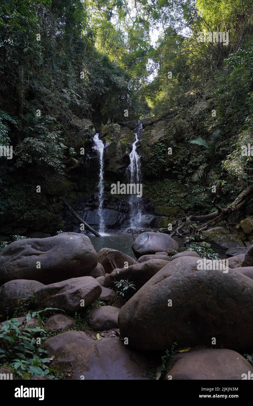 A vertical shot of a thin waterfall flowing down huge rocks Stock Photo ...