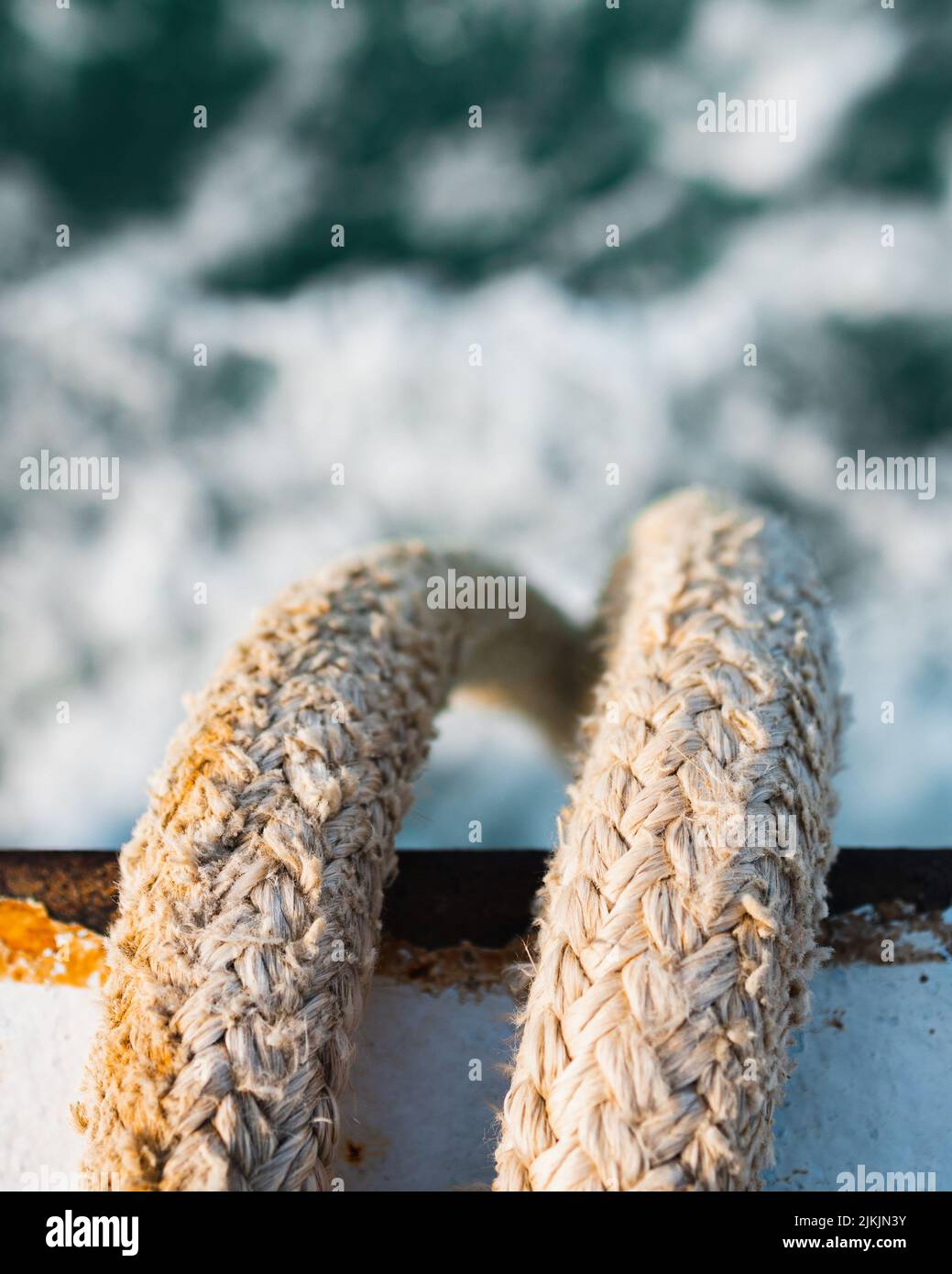 A vertical close-up shot of a thick rope leaning on a metallic pipe on ...