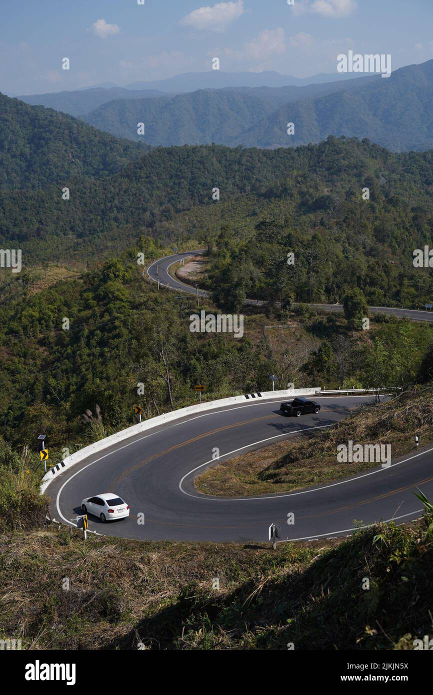 A vertical shot of cars driving on a curved highway surrounded by trees ...