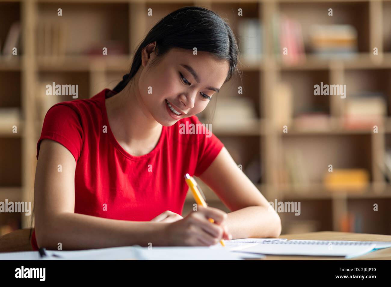 Smiling smart young chinese woman student doing homework, preparing to ...