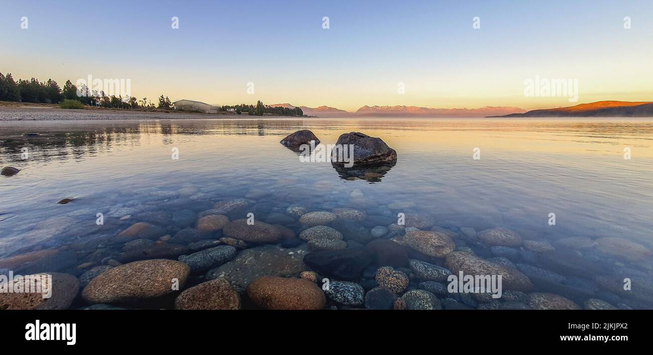 A beautiful panoramic shot of a crystal clear lake with visible stones ...