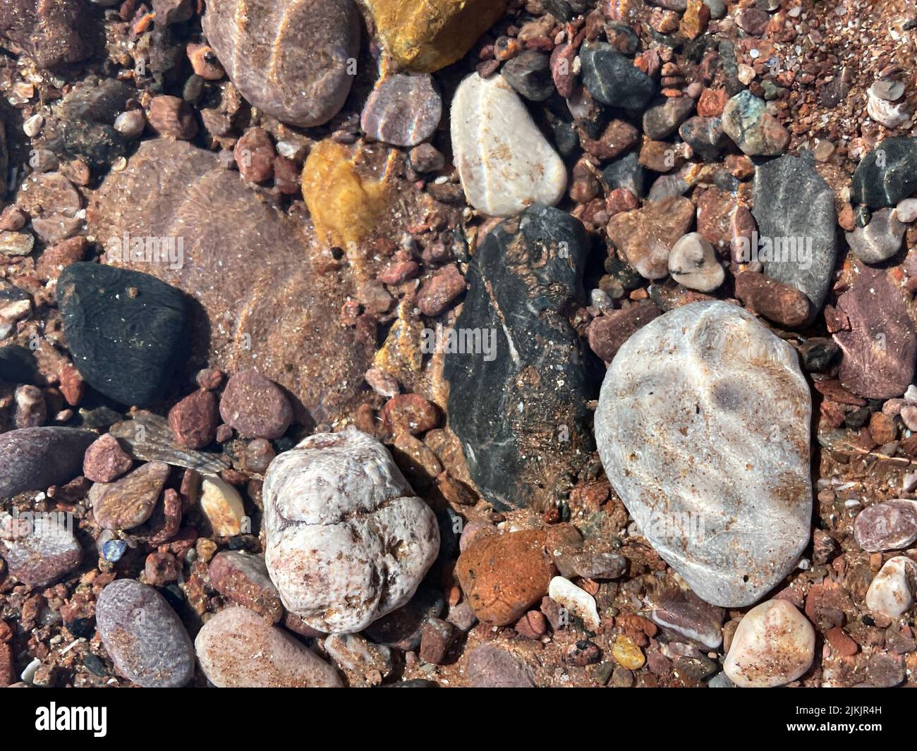 Colourful stones and pebbles in rock pool with sunlight reflections ...