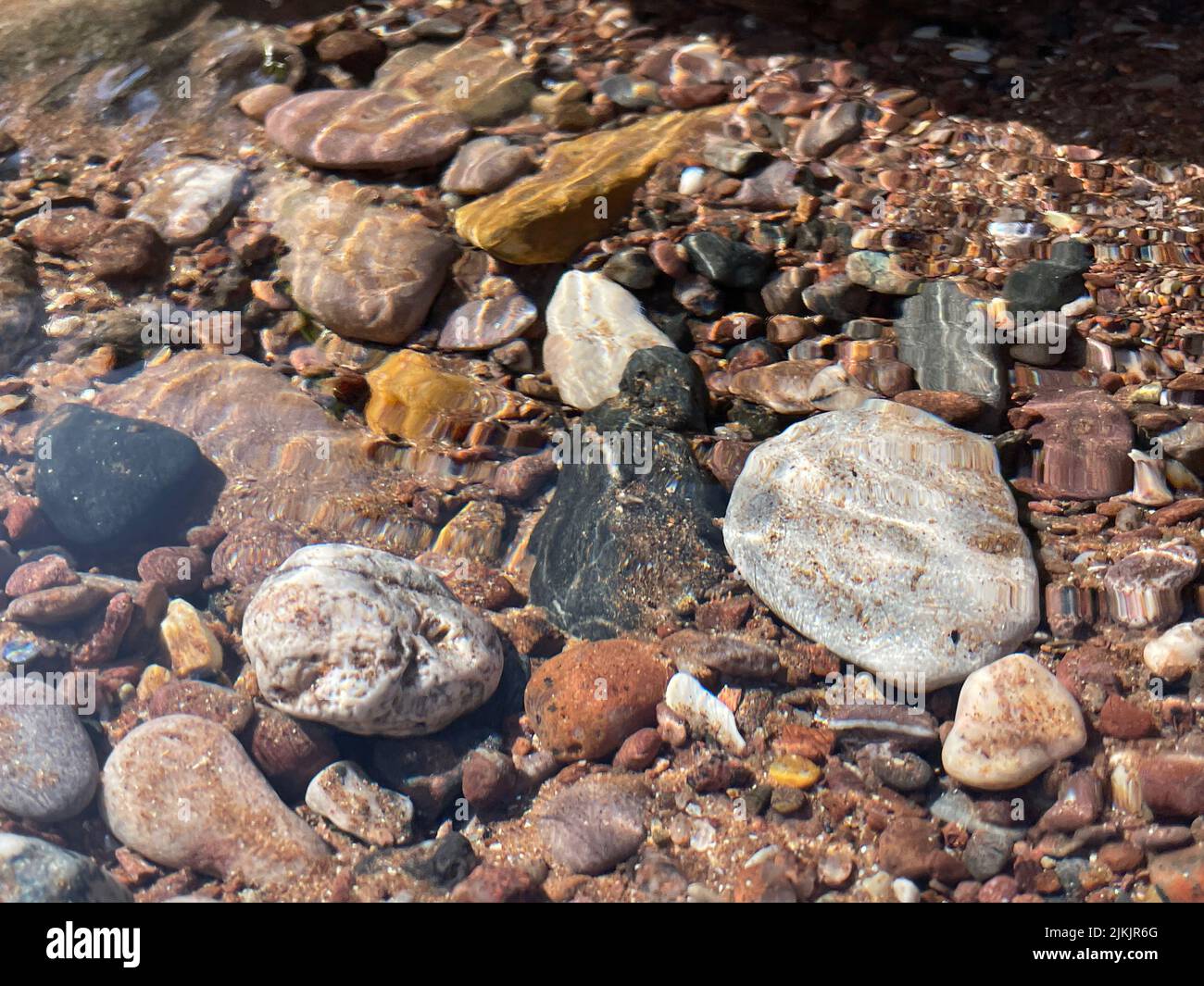 Colourful stones and pebbles in rock pool with sunlight reflections ...