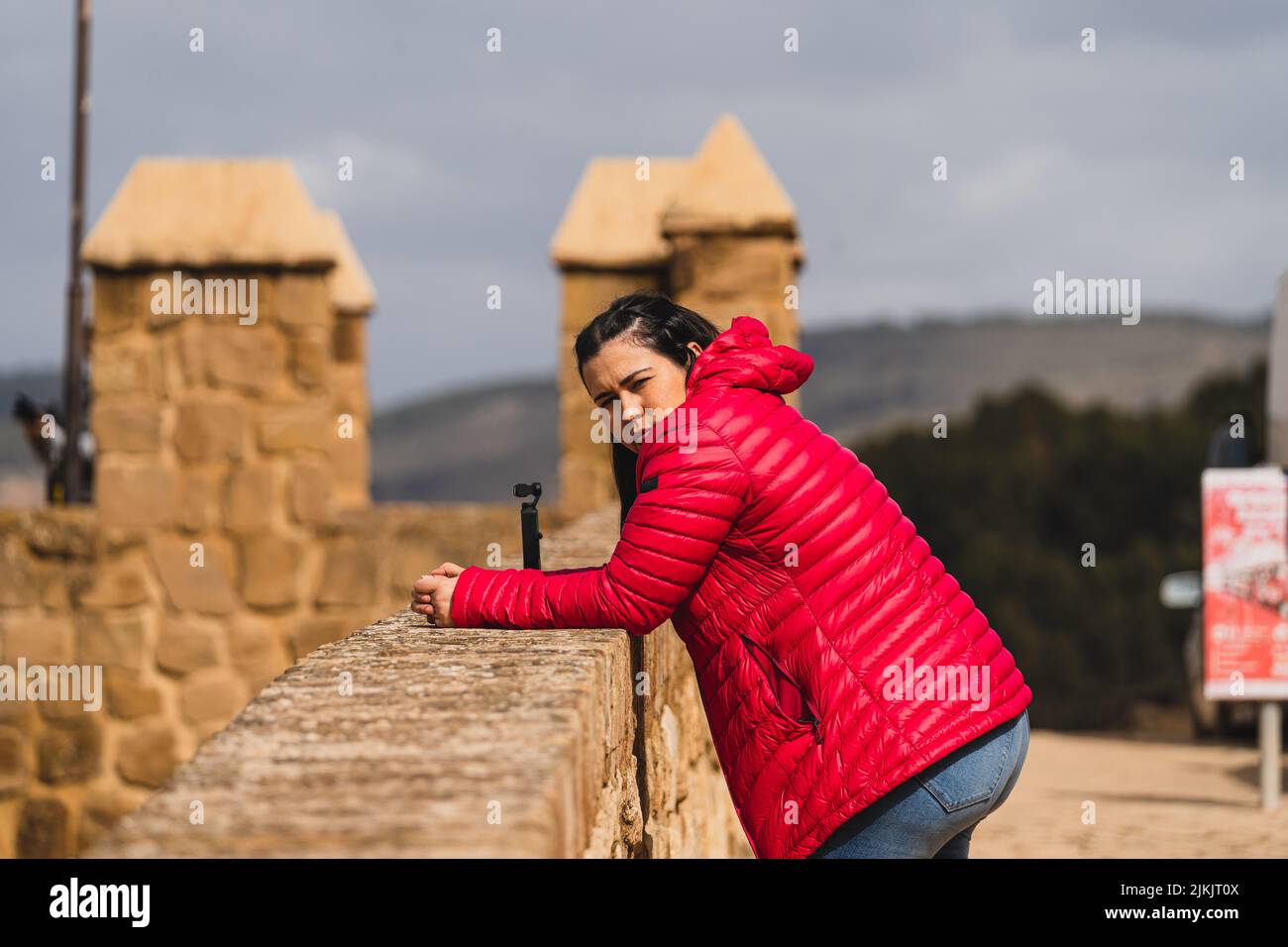 A young tourist female in a red jacket looking over the view from a ...