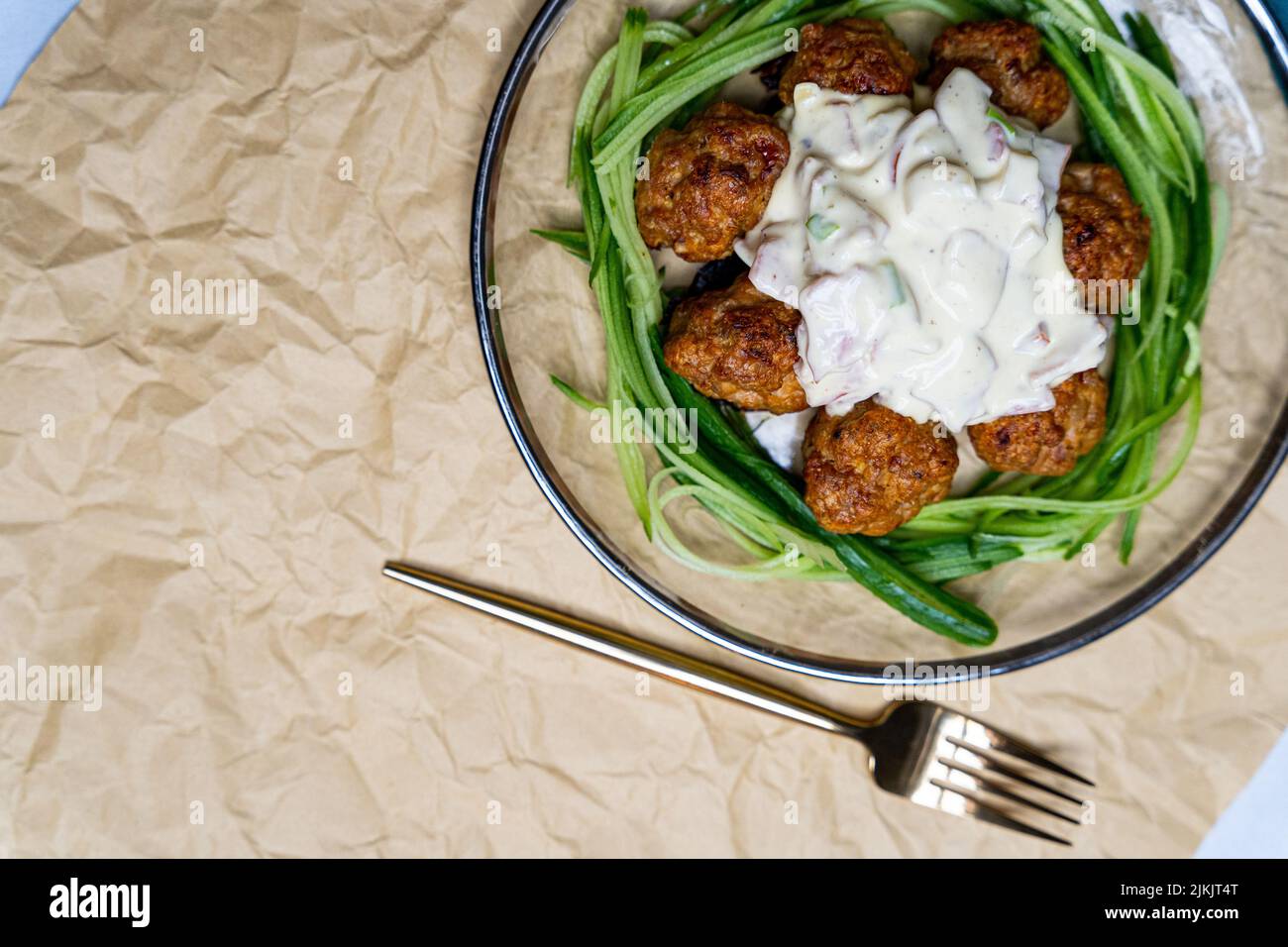 A top view of meatballs with white sauce and cucumber noodles on folded ...