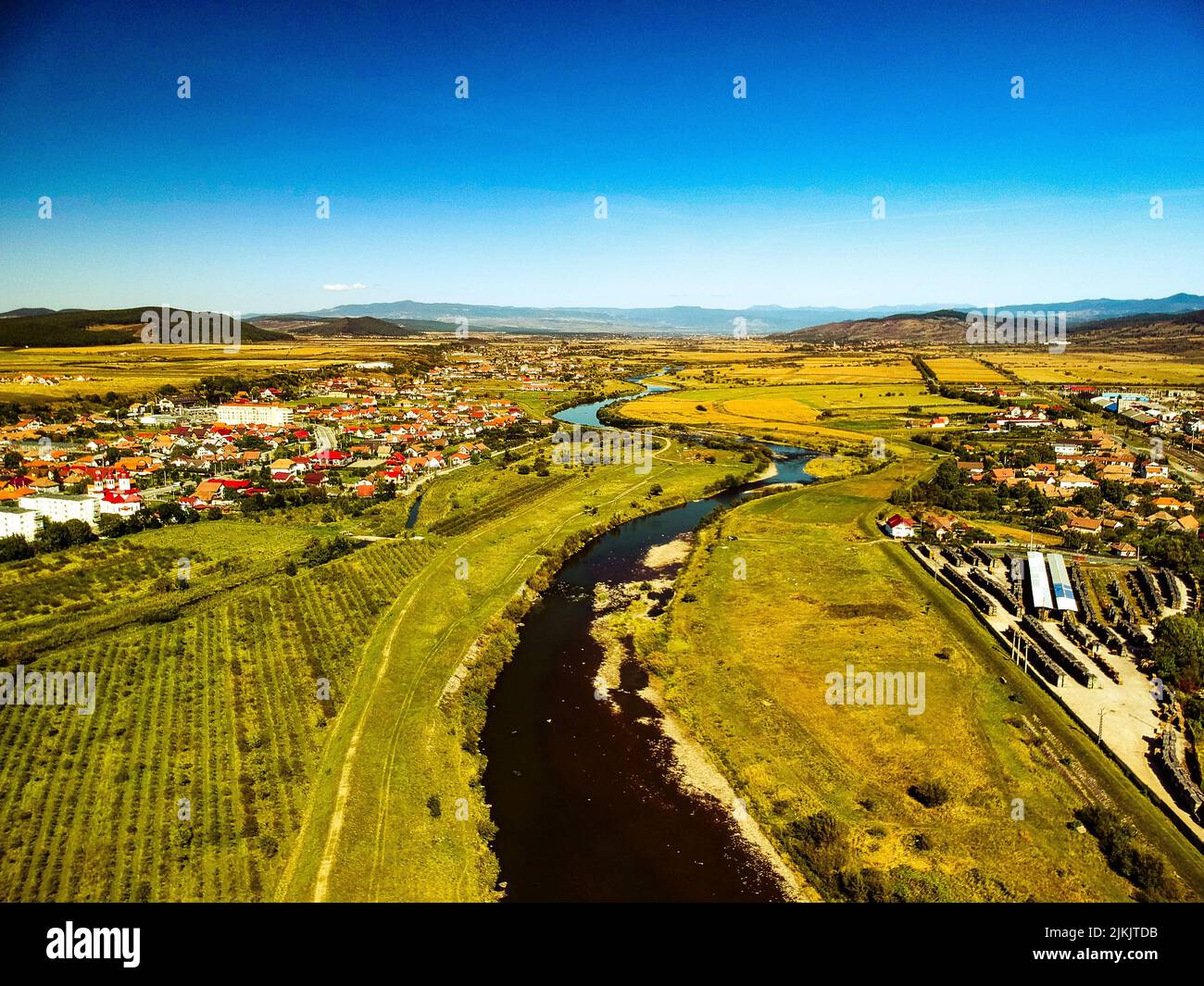 An aerial view of a flowing river surrounded by green fields in Romania ...