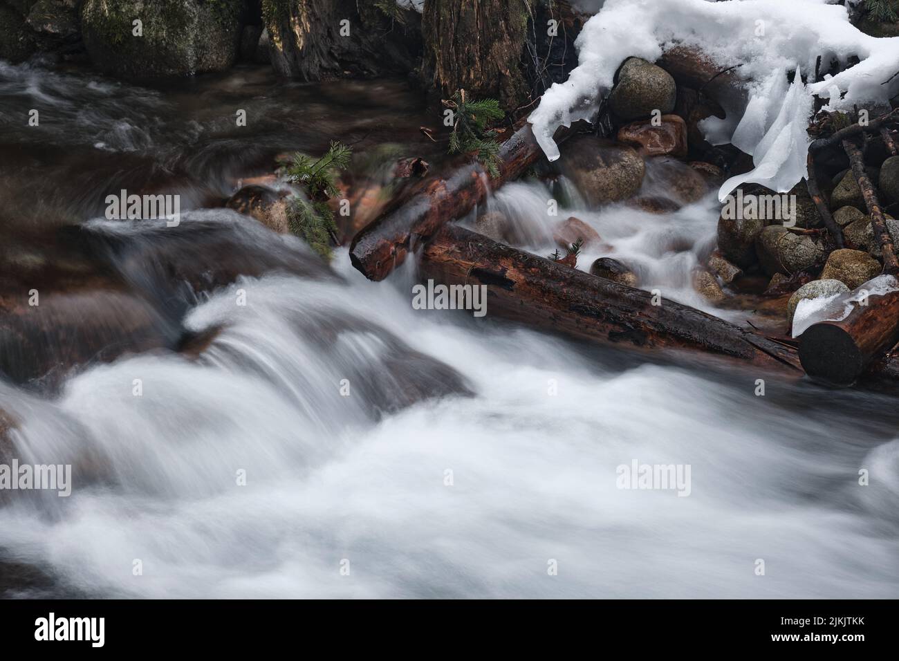 A waterfall with a fast-flowing river between mountain rocks and snow ...