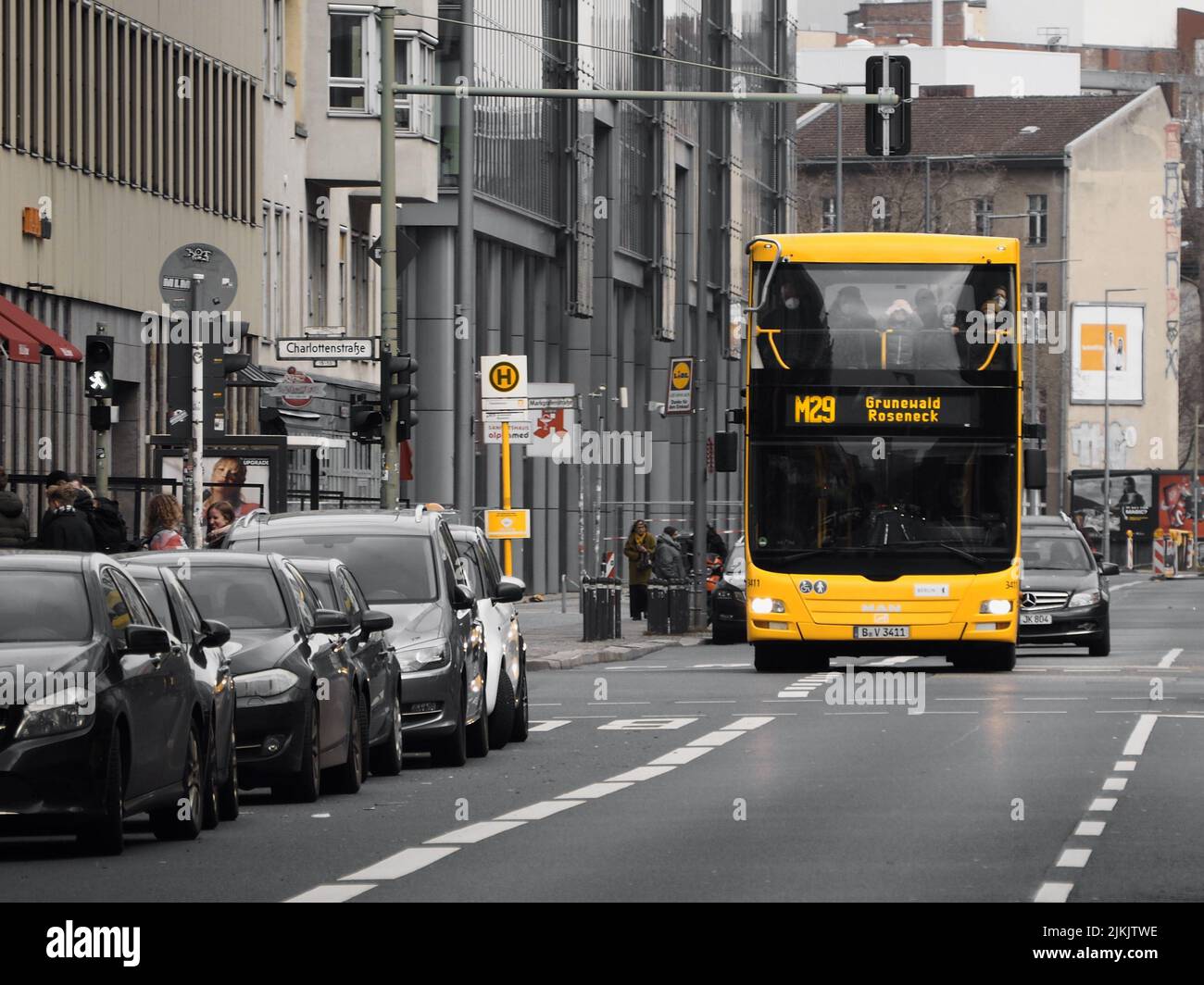 A big yellow public bus crossing the street next to the luxurious cars ...