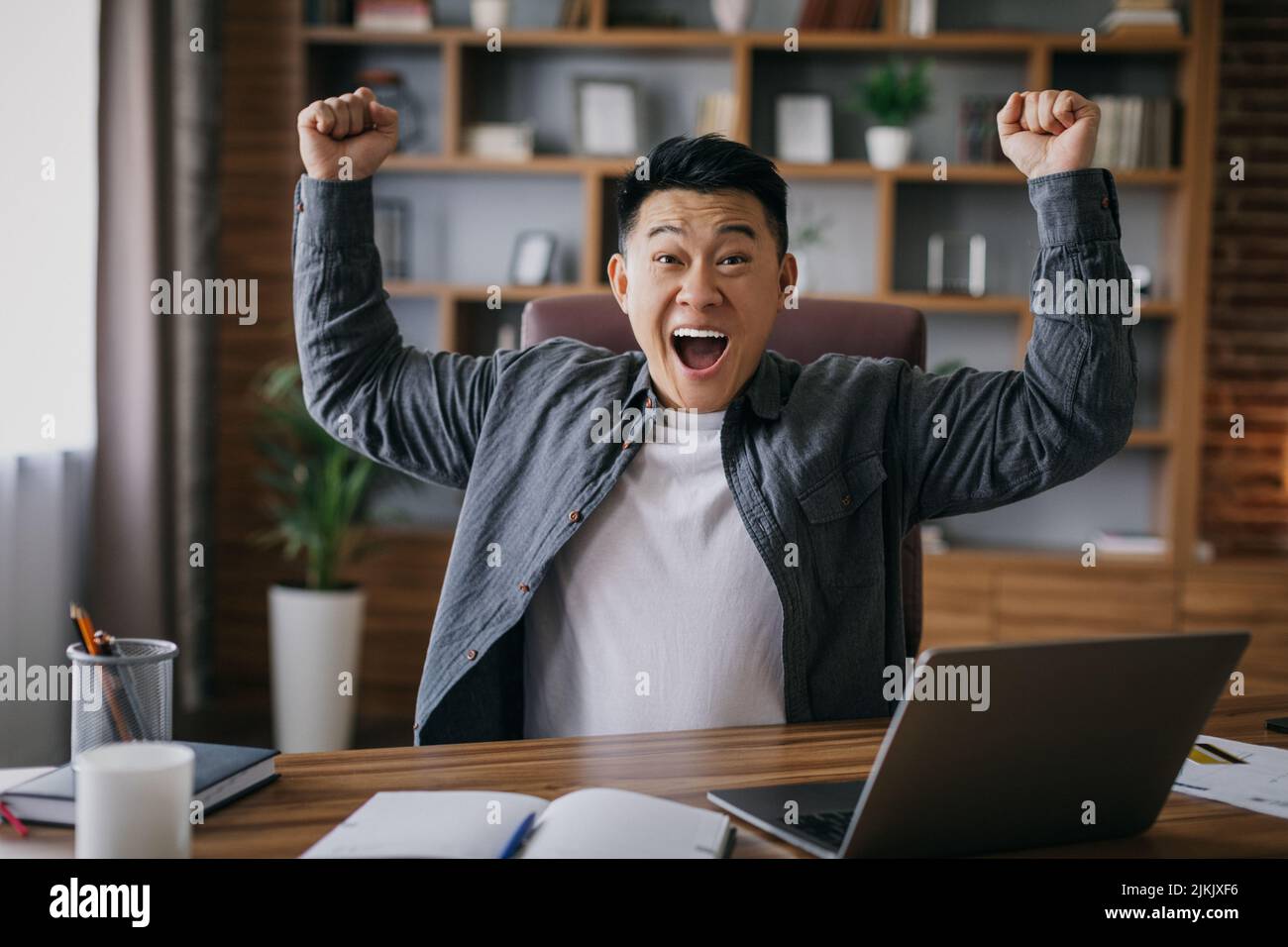 Glad excited adult asian businessman with open mouth raises hands up ...