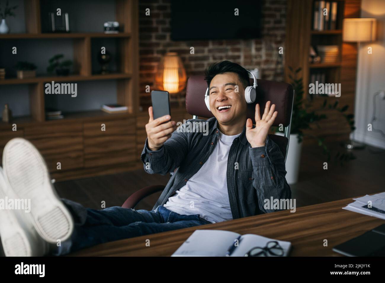 Happy middle aged asian male in headphones rest, has video call on ...