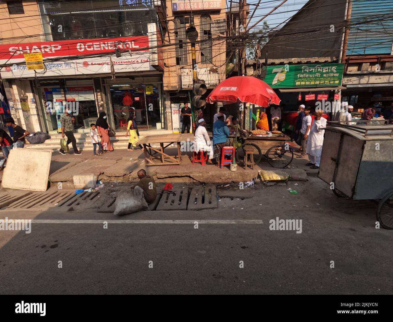 A dirty sidewalk with street food vendors on the street of Dhaka City ...
