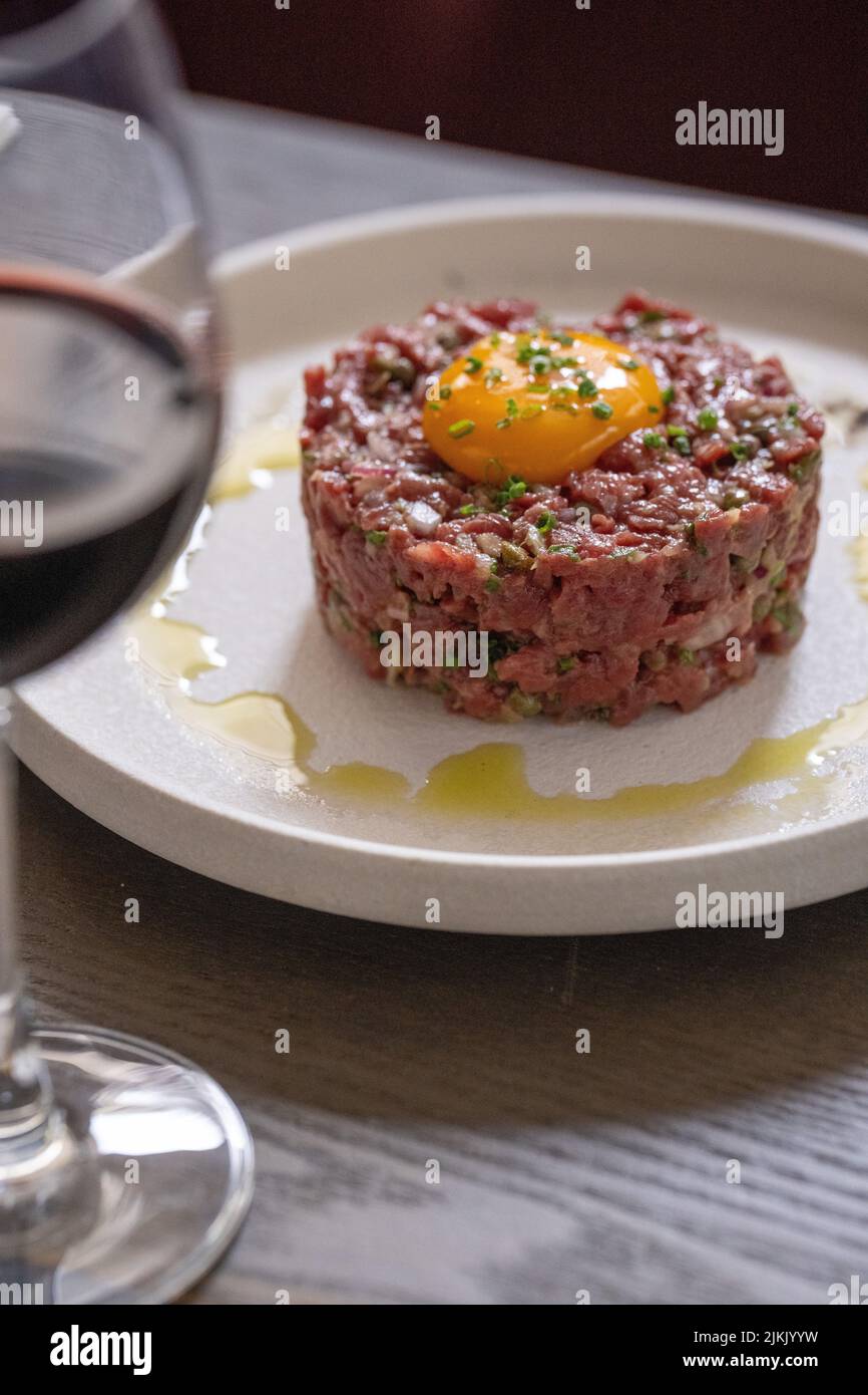 A vertical selective focus of a steak tartare with egg yolk on a white ...