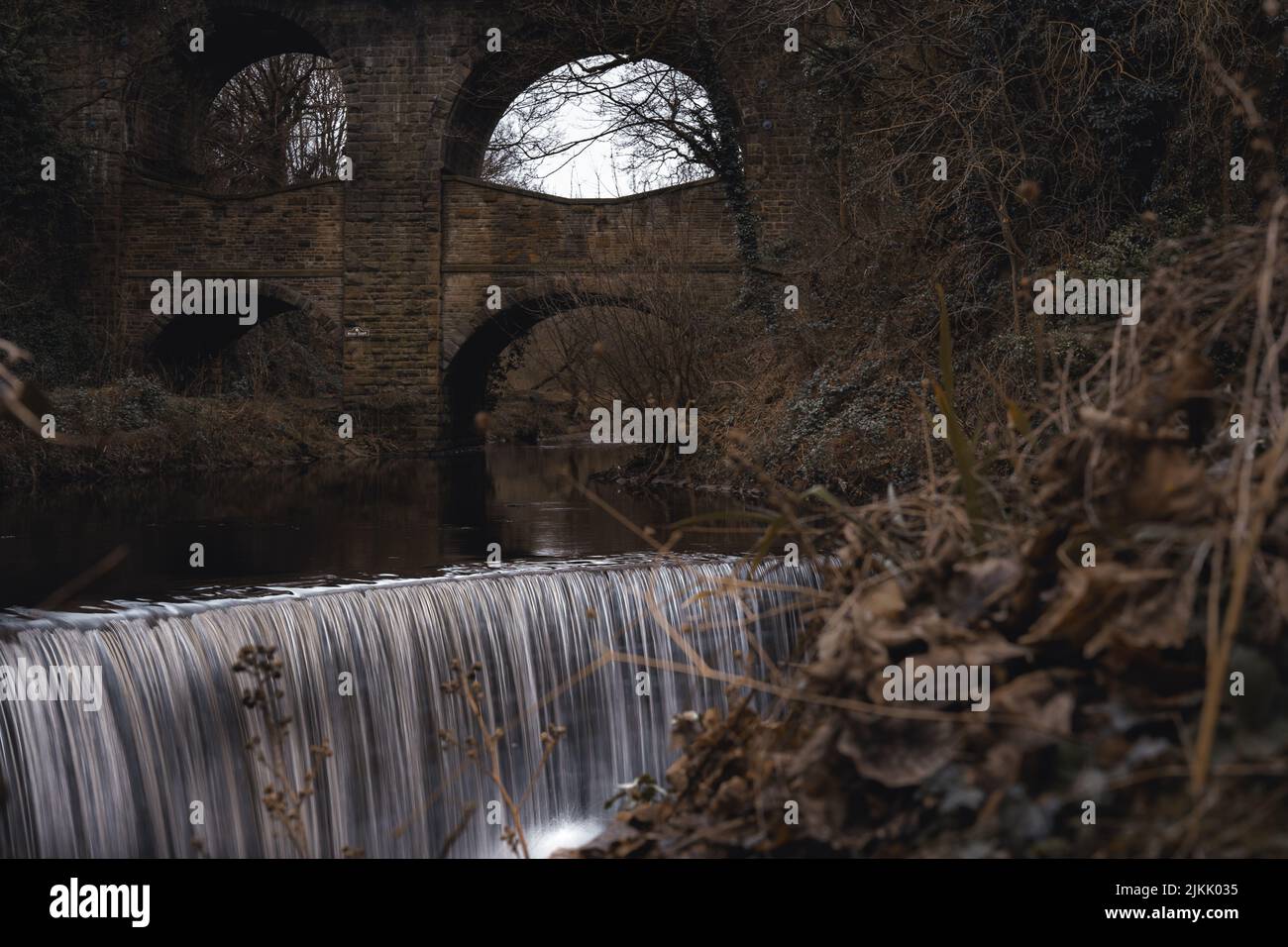 A small waterfall with arched bridge in the background Stock Photo - Alamy