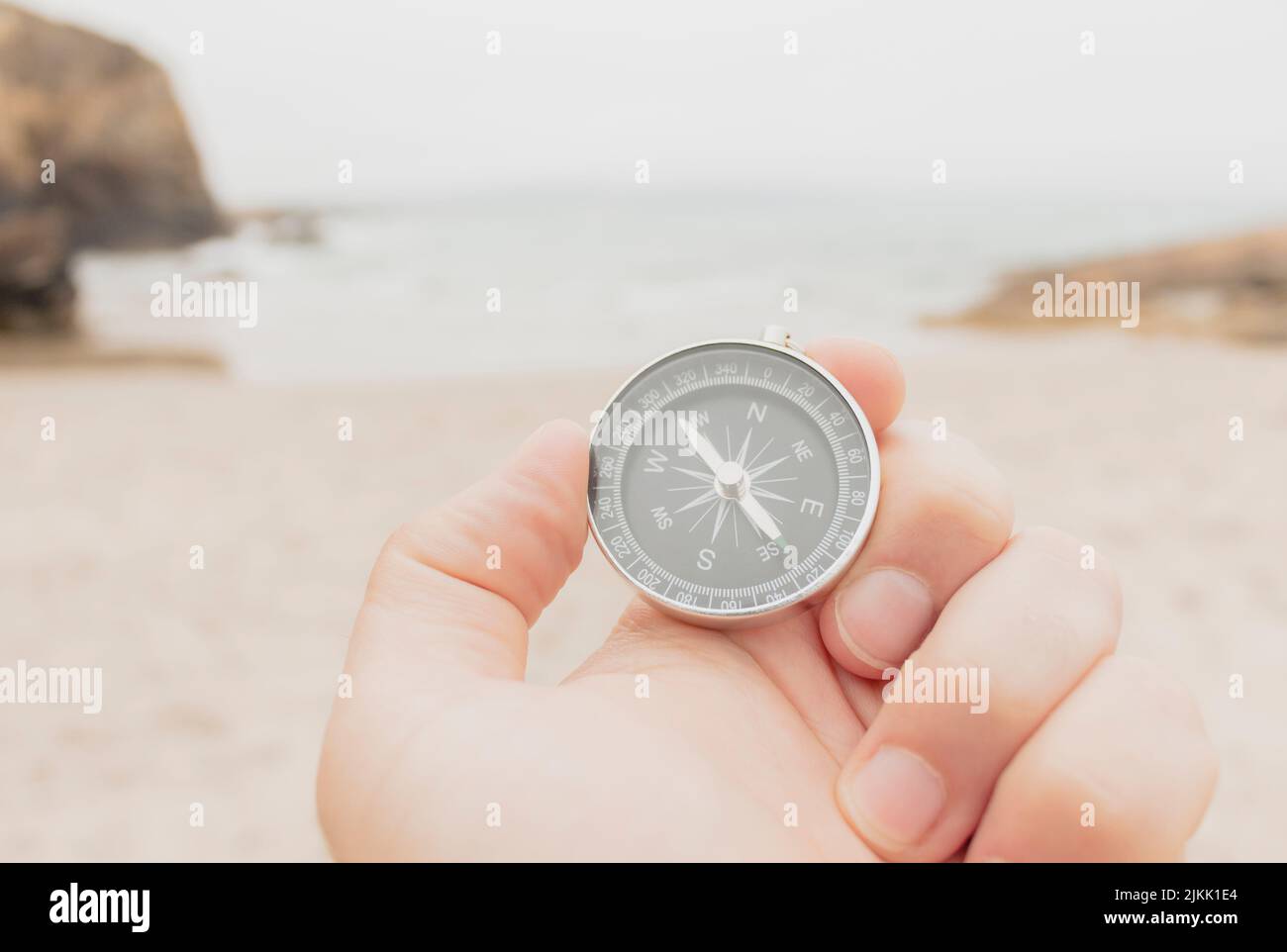 Closeup, hand holding an analog compass on the beach in front of the ...