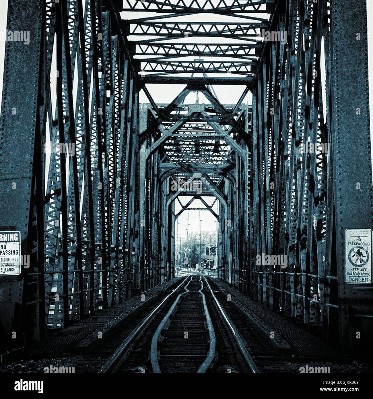 A grayscale shot of the railroad bridge with warning signs on its ...