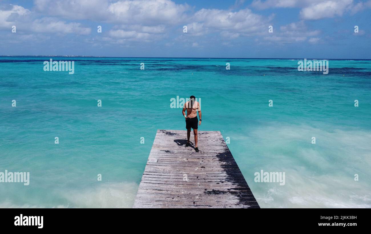A man standing on wooden bridge and his back to the sea in Tulum Beach ...