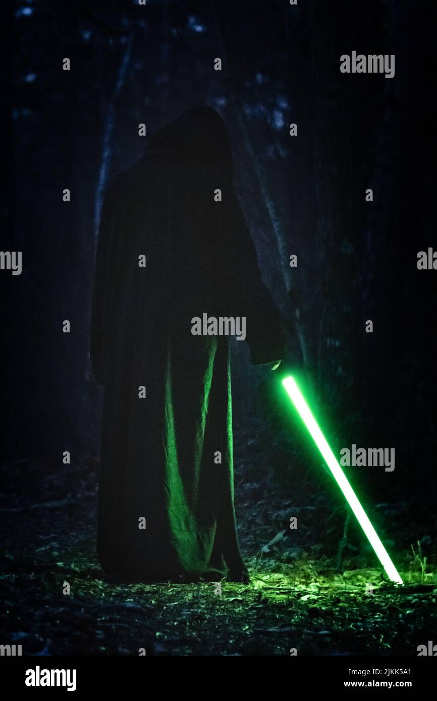 A man in a black mantle holding a green neon sword in the hand. Dark ...