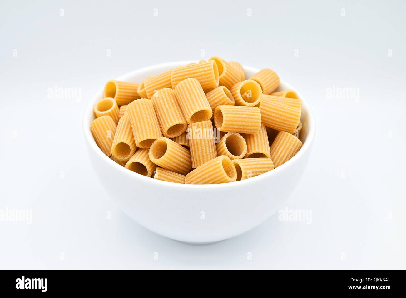 A closeup of raw rigatoni pasta in a white bowl on a white background ...