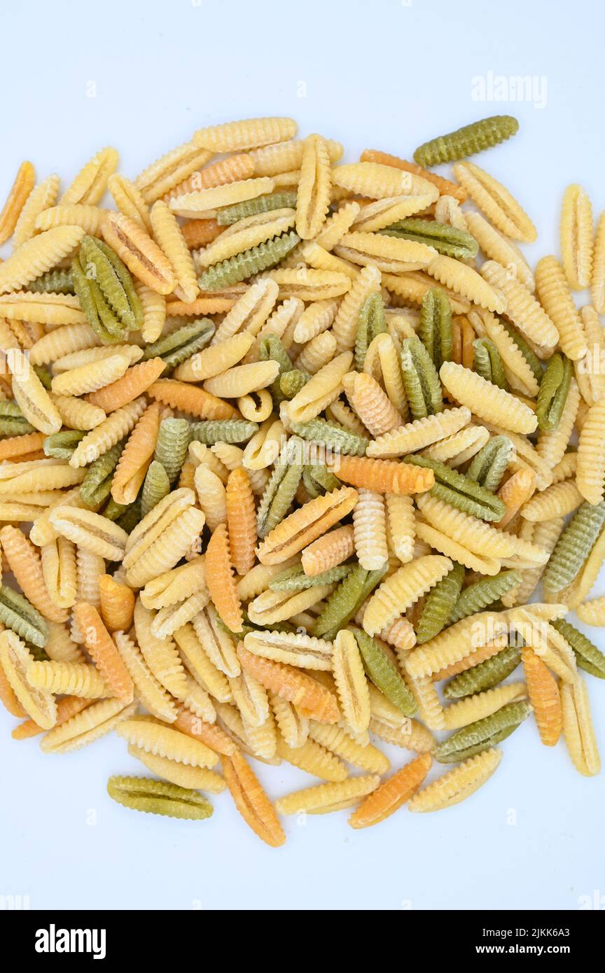 A vertical closeup of colorful raw malloreddus pasta on a white surface ...