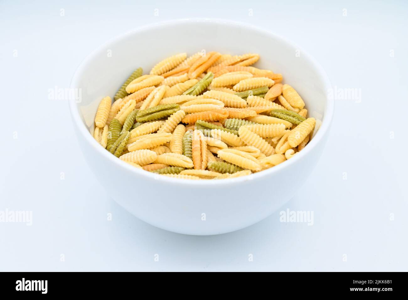 A closeup of colorful raw malloreddus pasta in a bowl on a white ...