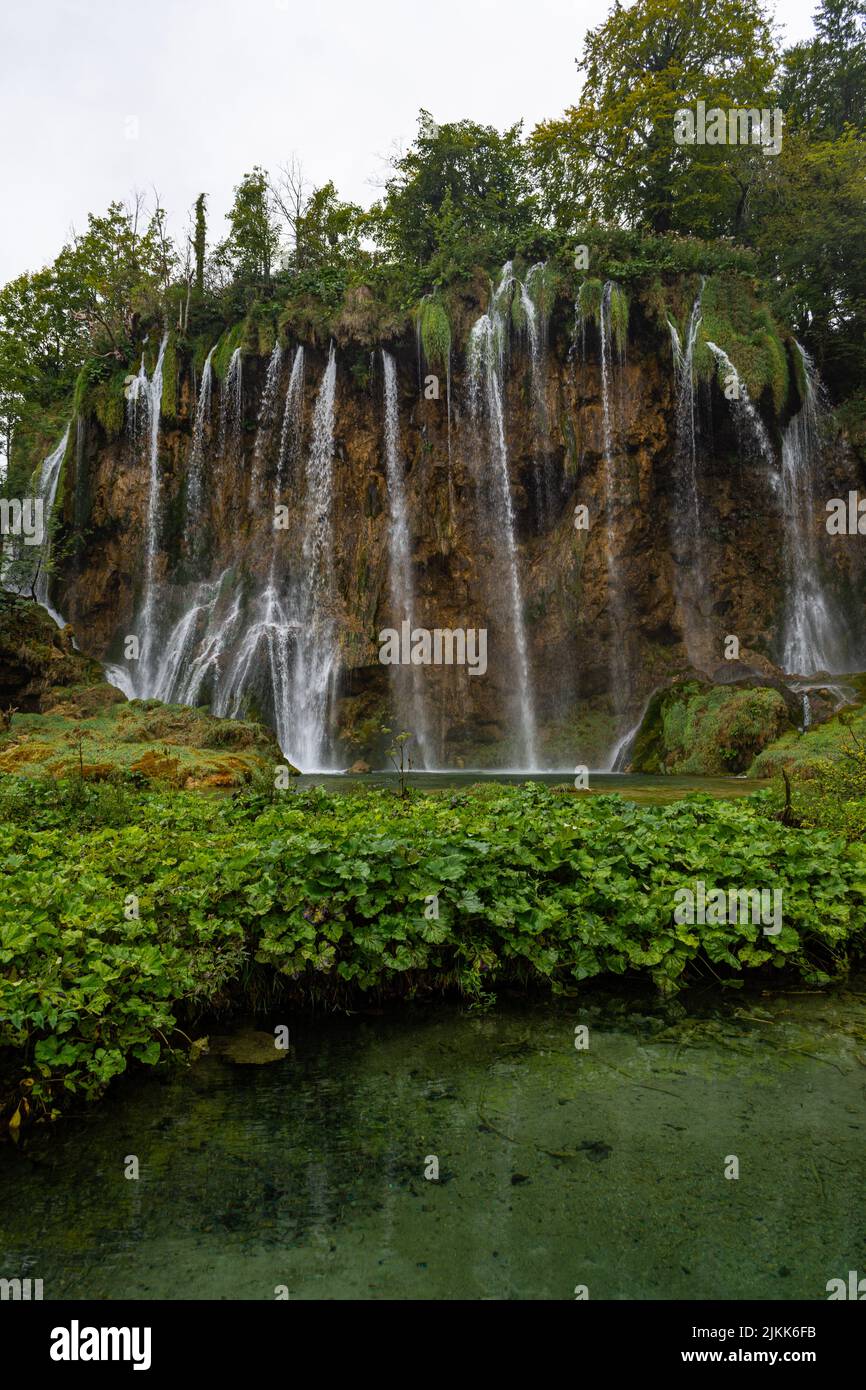 A vertical view of a scenic waterfall and a calm lake surrounded with ...