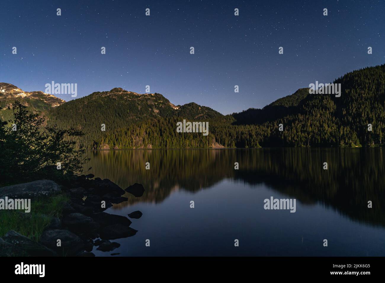 A scenic view of evergreen hills reflecting on a calm lake Stock Photo ...