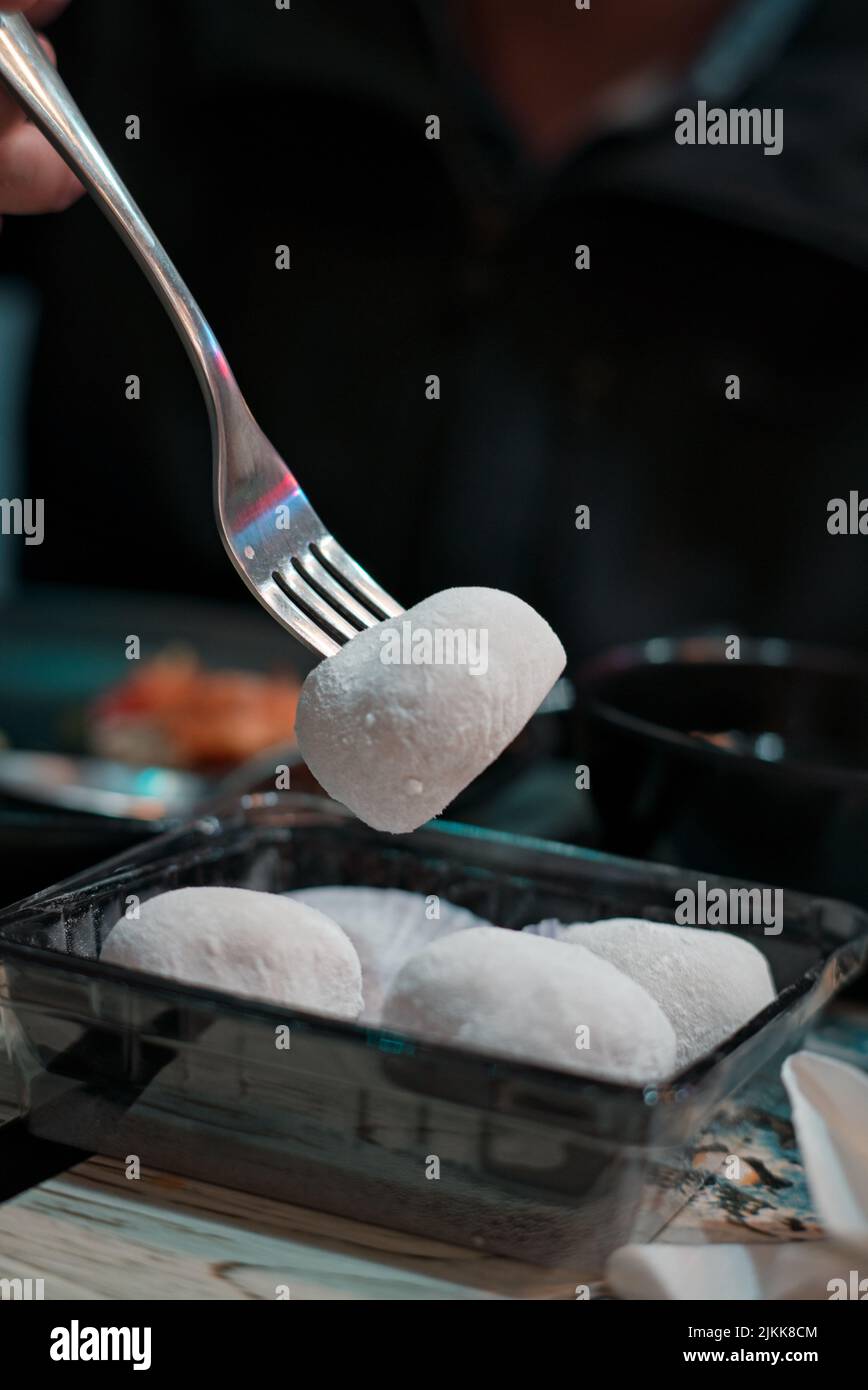 A vertical shot o a delicious mochi on a fork above a bowl of mochi ...
