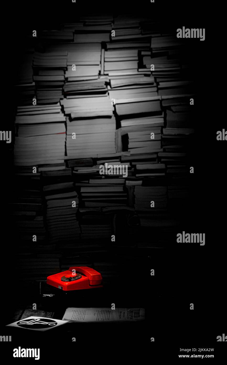 A vertical shot of a red traditional landline telephone with piles of ...