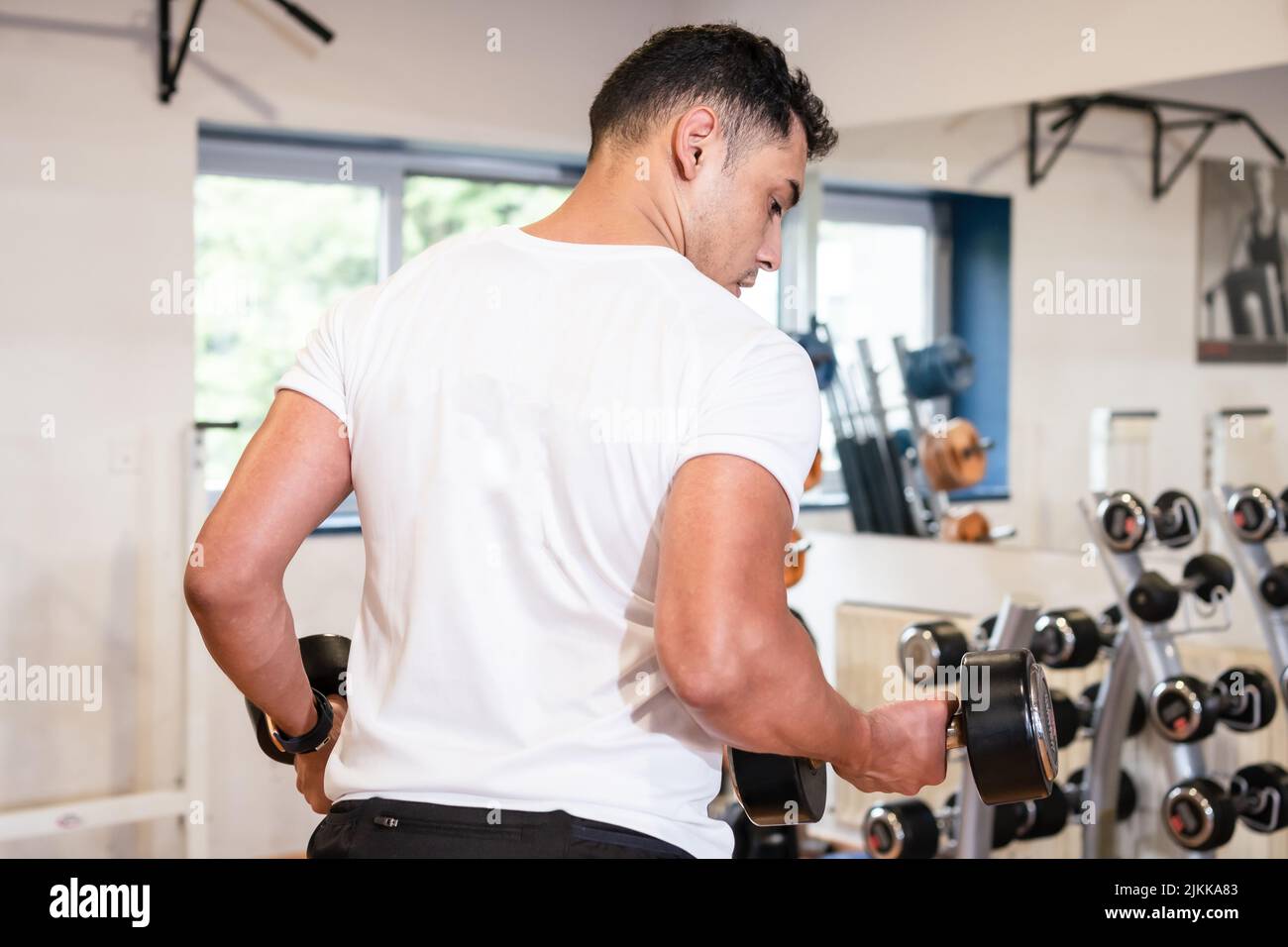A caucasian man from the back in the gym in a white t-shirt lifting ...