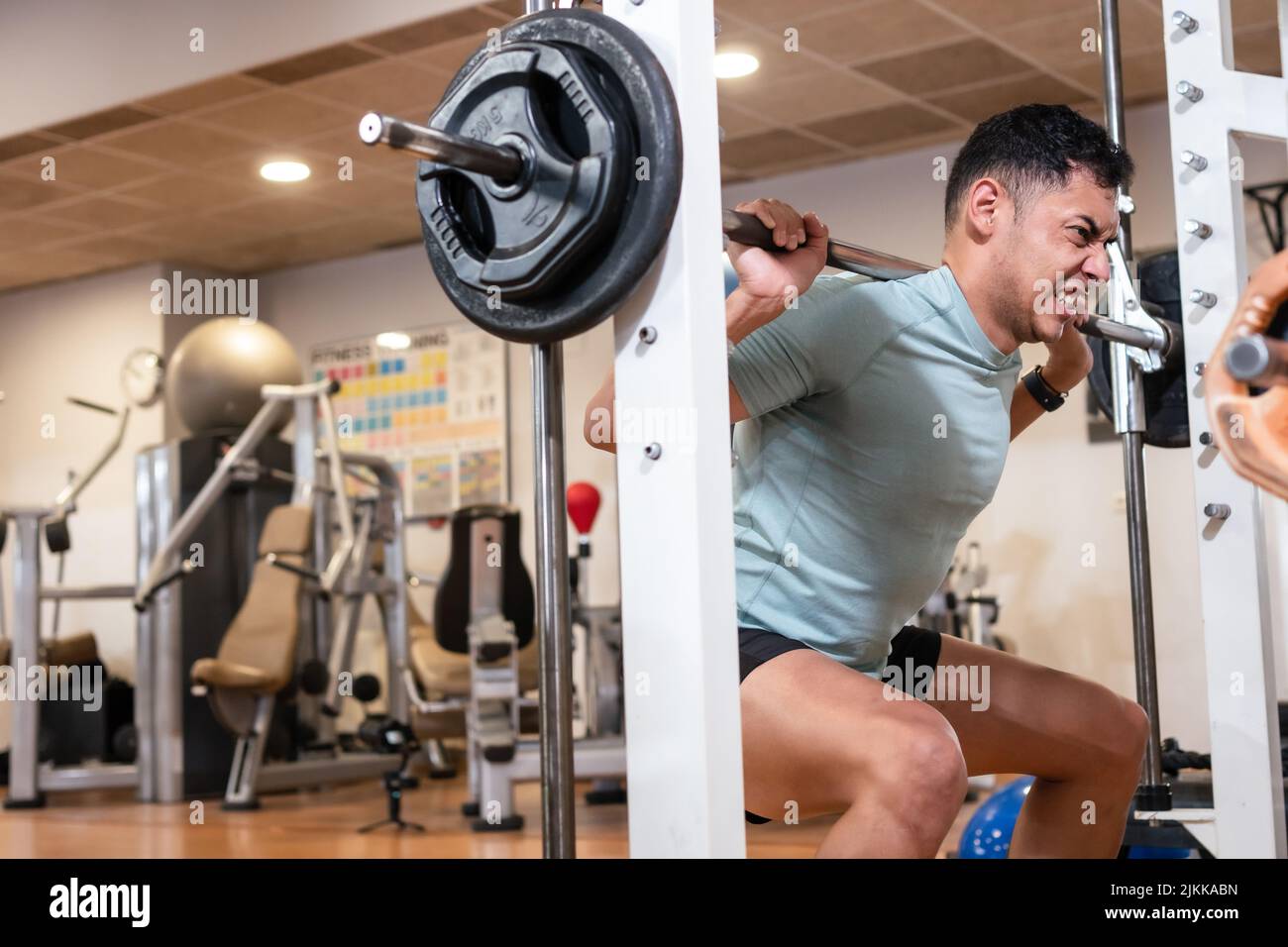 A caucasian man in the gym lifting weights with a lot of effort ...