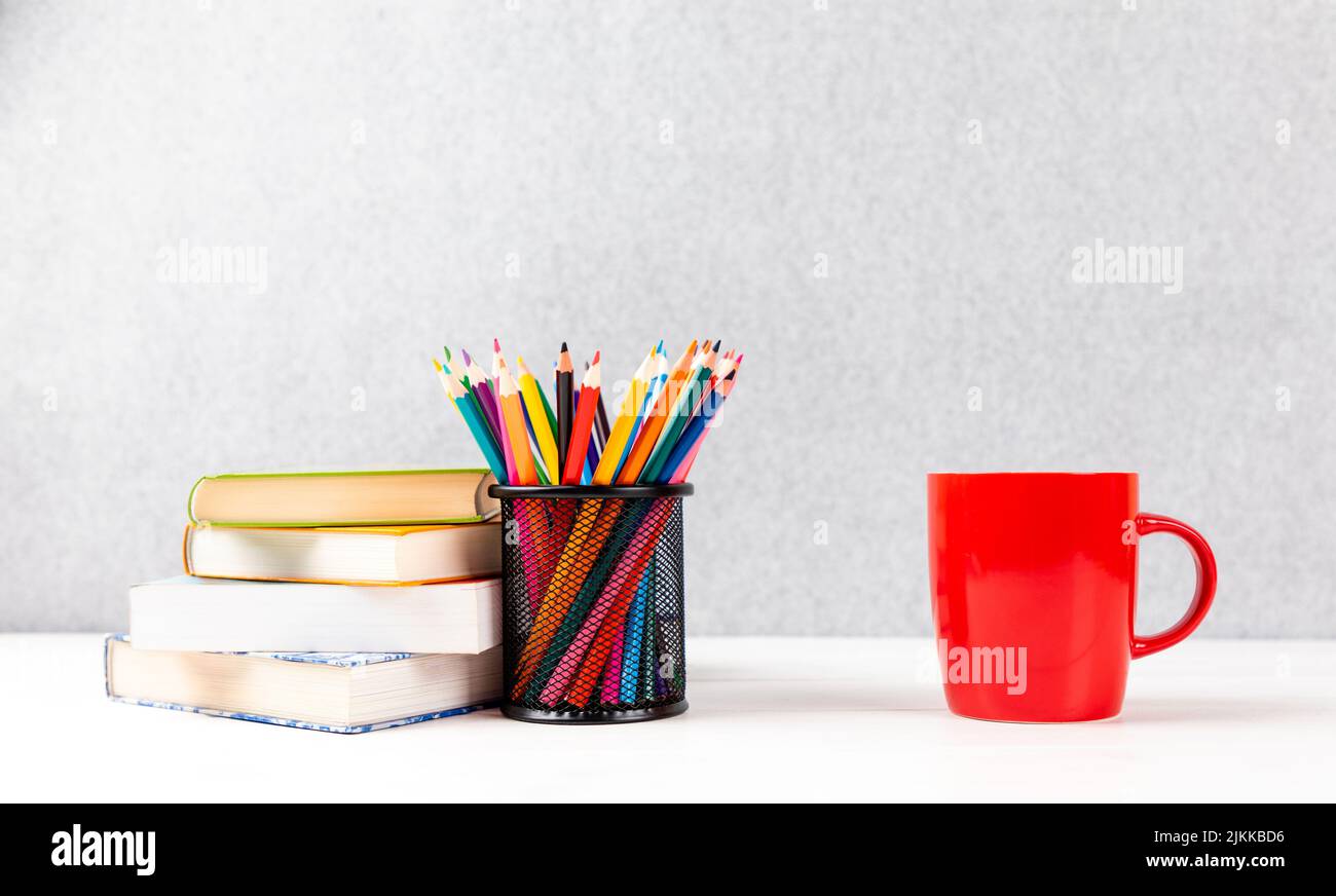 colorful pencils, books and red cup on a desk with gray background and ...