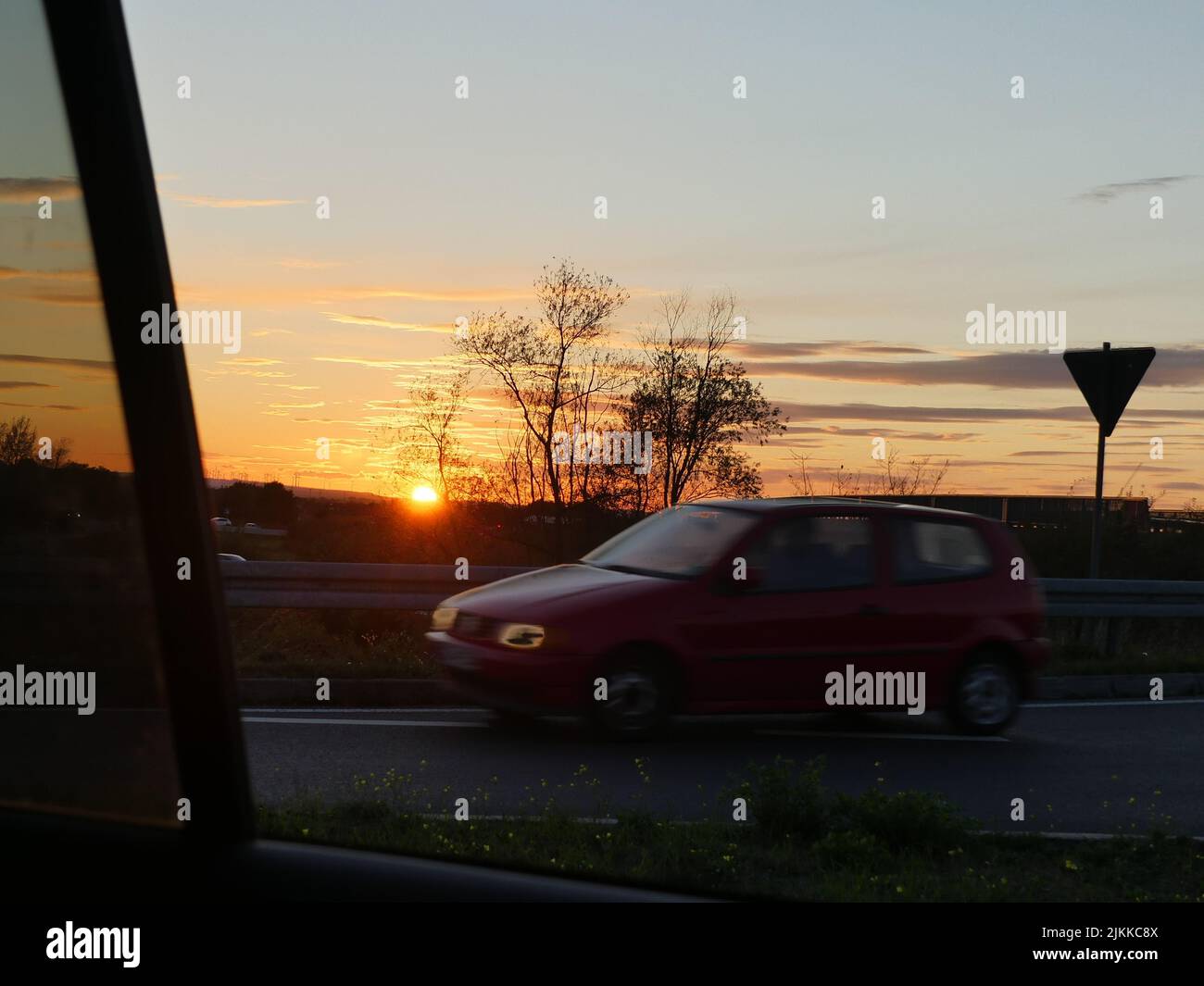 A red car on the road in the time of sunset with trees in the ...