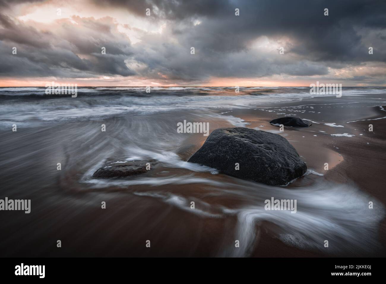 A beautiful view of the sea with many rocks under a cloudy sunset sky ...