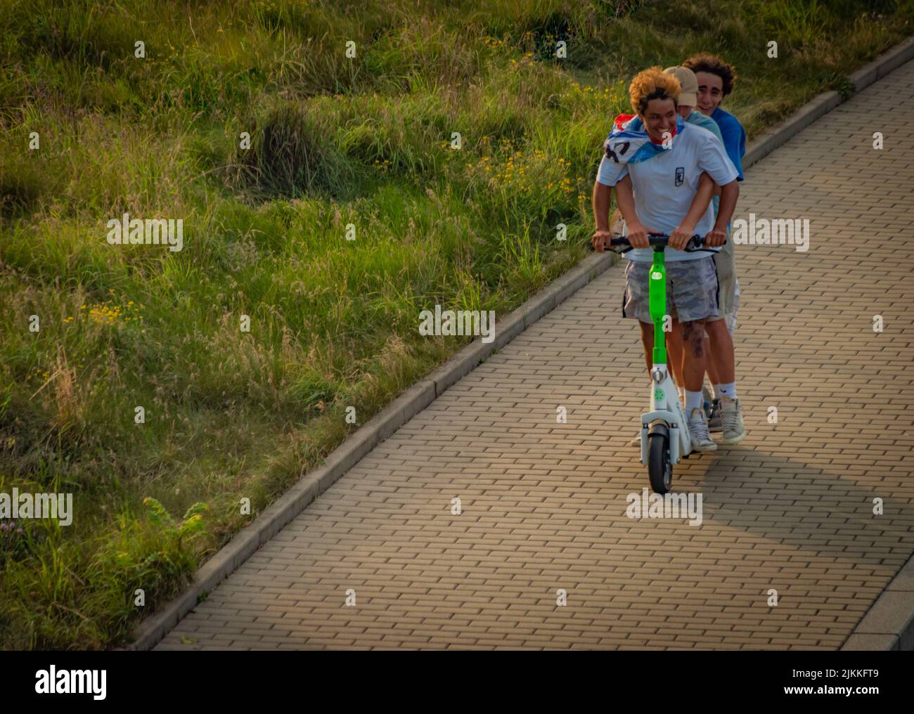 Three boys on electric scooter on pavement near bridge over Vltava ...