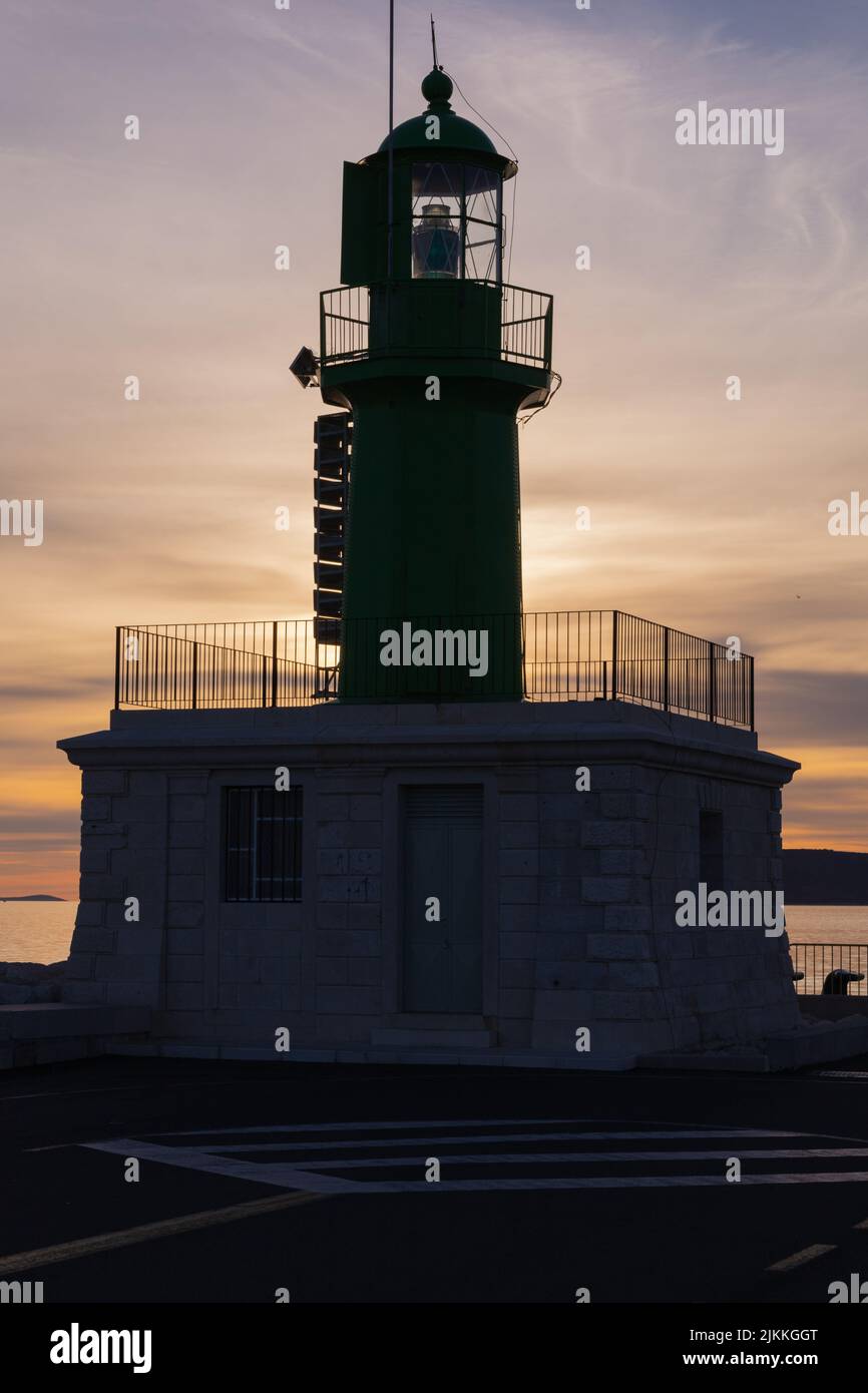 A beautiful vertical shot of a backlit lighthouse silhouette with a ...