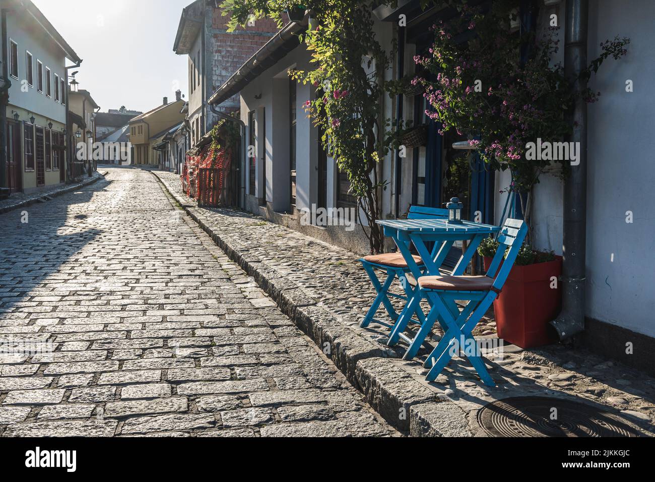 A beautiful view of blue wooden chairs and a table of an outdoor cafe on a cobblestone street ...