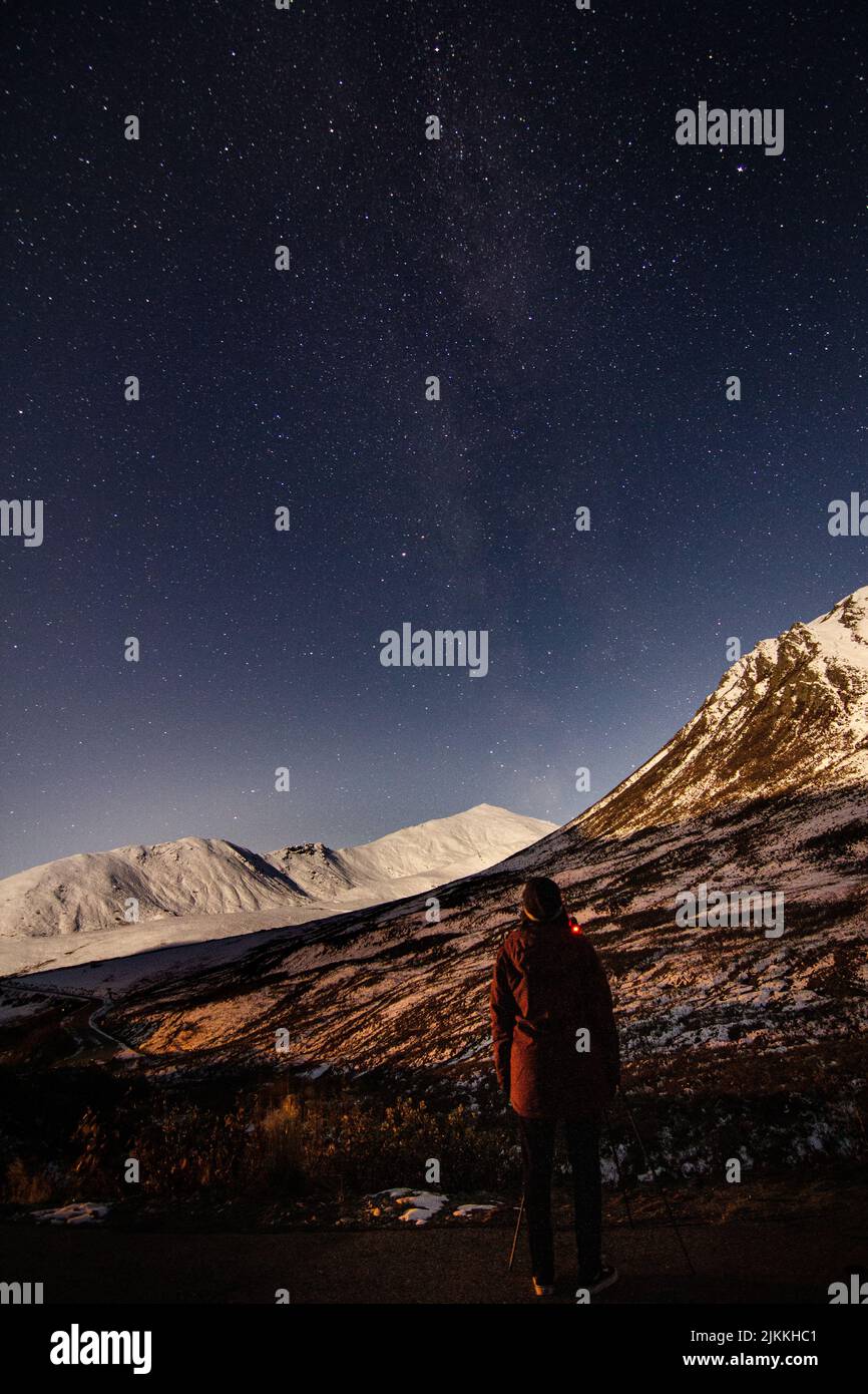 A vertical back view of a tourist with a tripod looking at the Milky ...