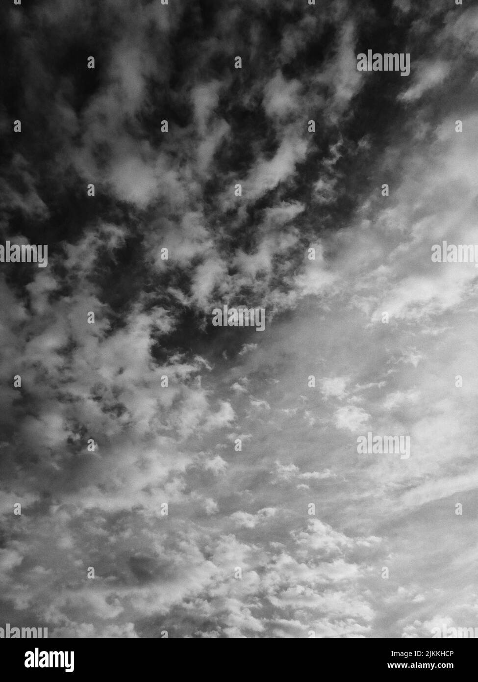 A vertical low angle grayscale shot of the sky with cumulus clouds ...